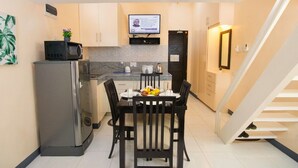 Uma cozinha compacta com mesa, cadeiras, geladeira, micro-ondas, televisão e escada.
