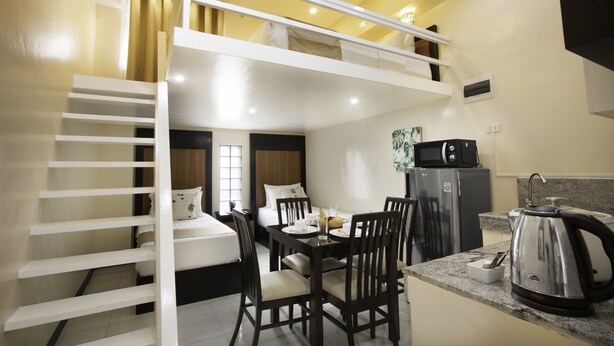Quarto de hotel pequeno com beliche, cozinha compacta, área de refeições e um cantinho de estar.
