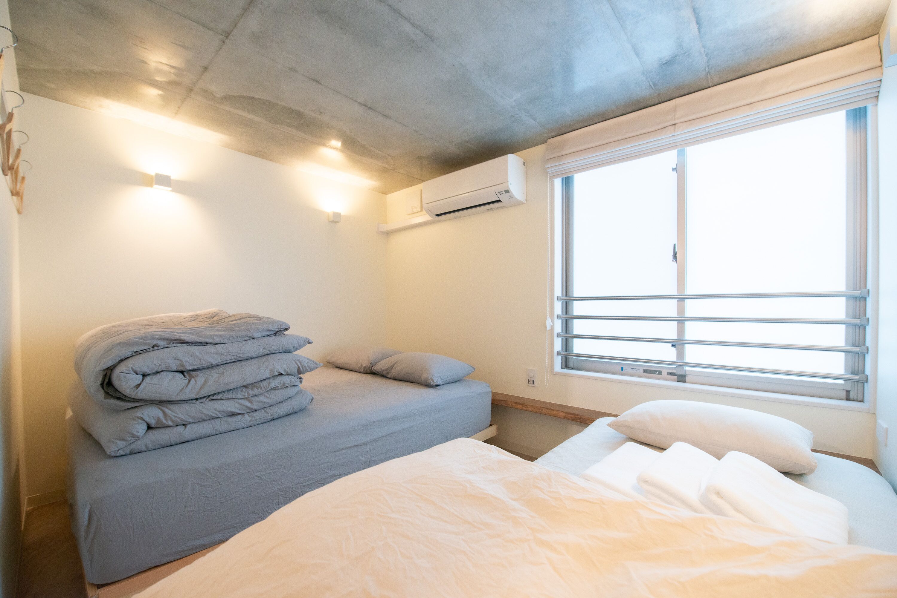Quarto com cama, janela com persianas, ar condicionado e luminária fixada na parede.