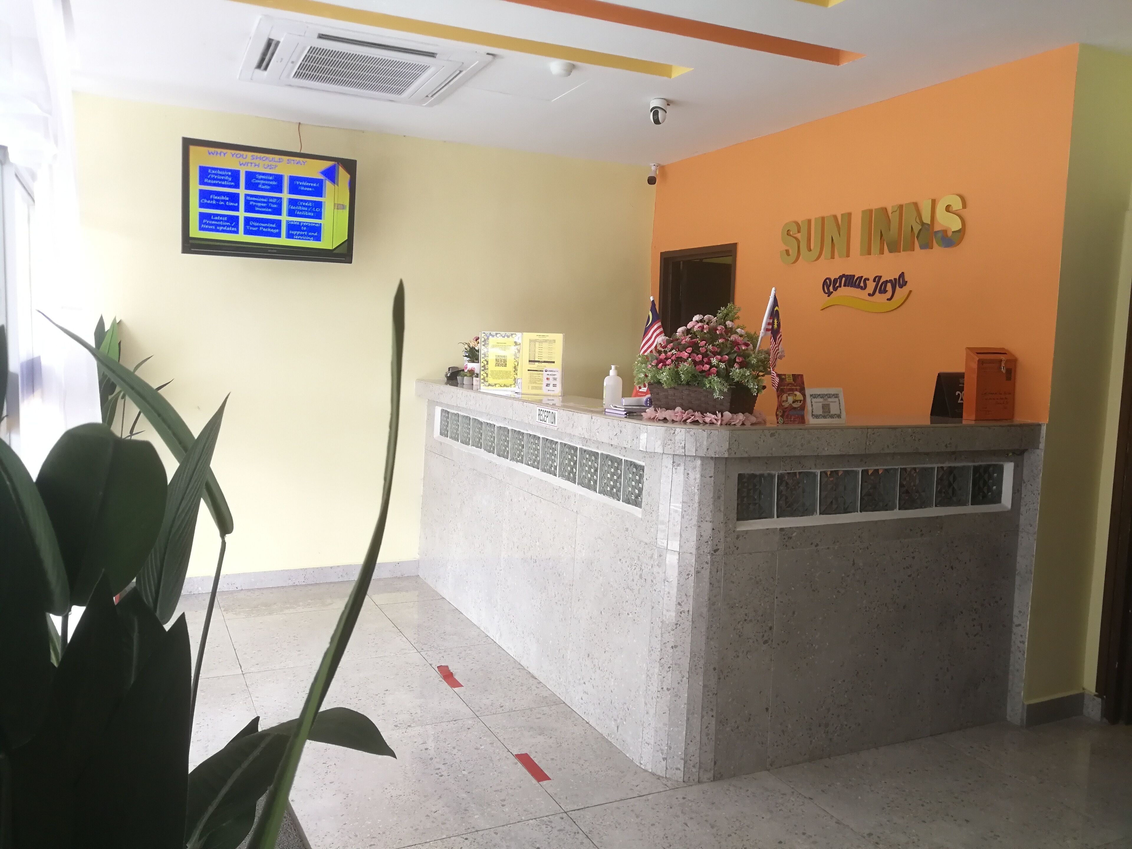 Balcão de recepção com uma placa indicando "SUN INNS" e uma tela digital exibindo informações.