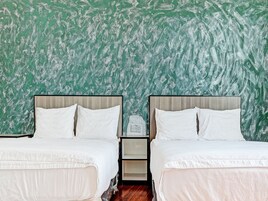 Quarto com duas camas, cada uma com roupa de cama branca e cabeceiras de madeira, diante de uma parede verde texturizada.
