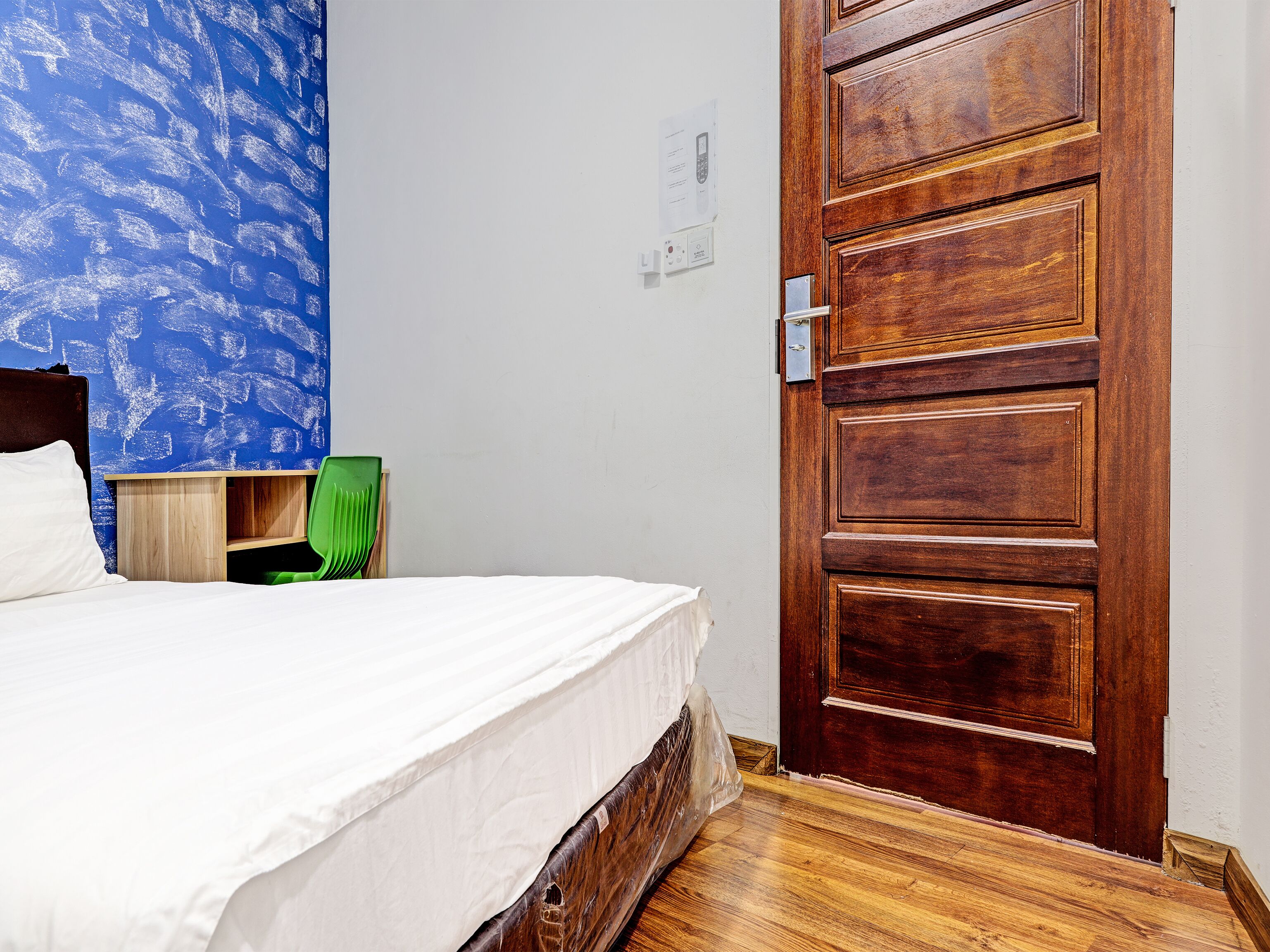 Quarto com cama, porta de madeira e parede azul com desenhos brancos.