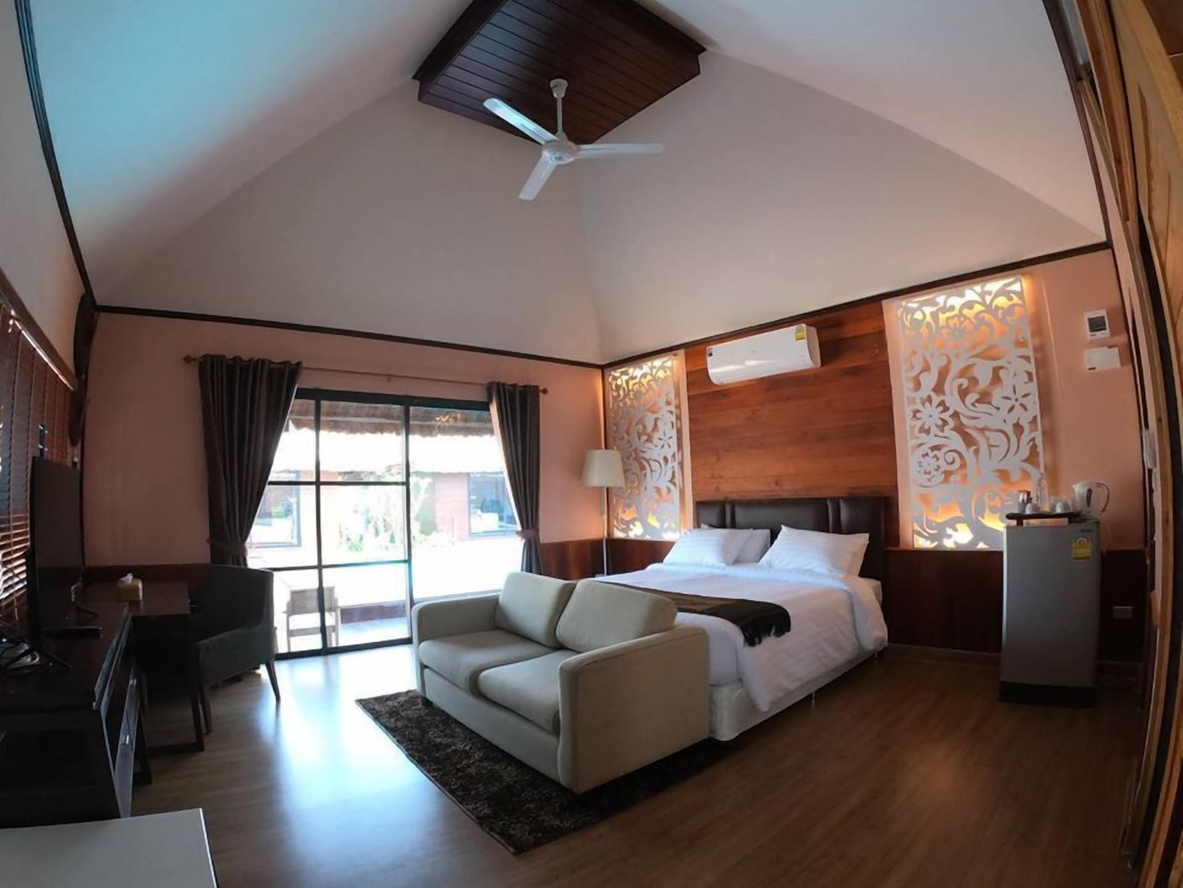 Quarto de hotel moderno com cama, sofá, escrivaninha e ventoinha no teto.