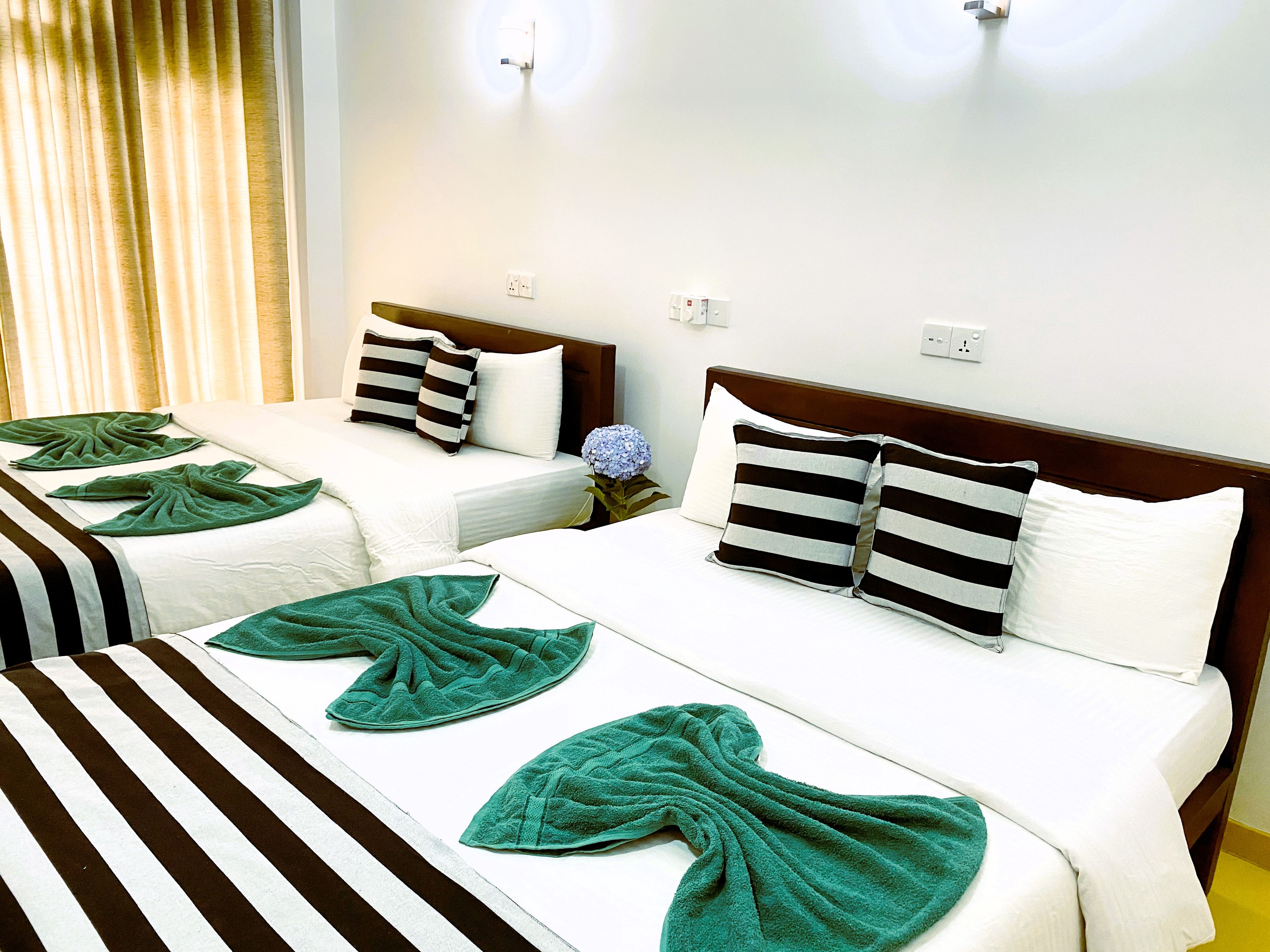 Quarto de hotel com duas camas, cada uma com colcha listrada e almofadas, e uma toalha verde na cama.