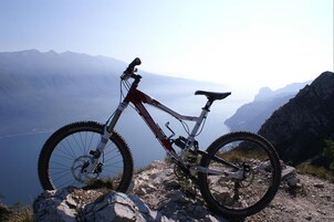 Uma bicicleta de montanha estacionada em terreno rochoso, com uma vista panorâmica de montanhas e um vale ao fundo.