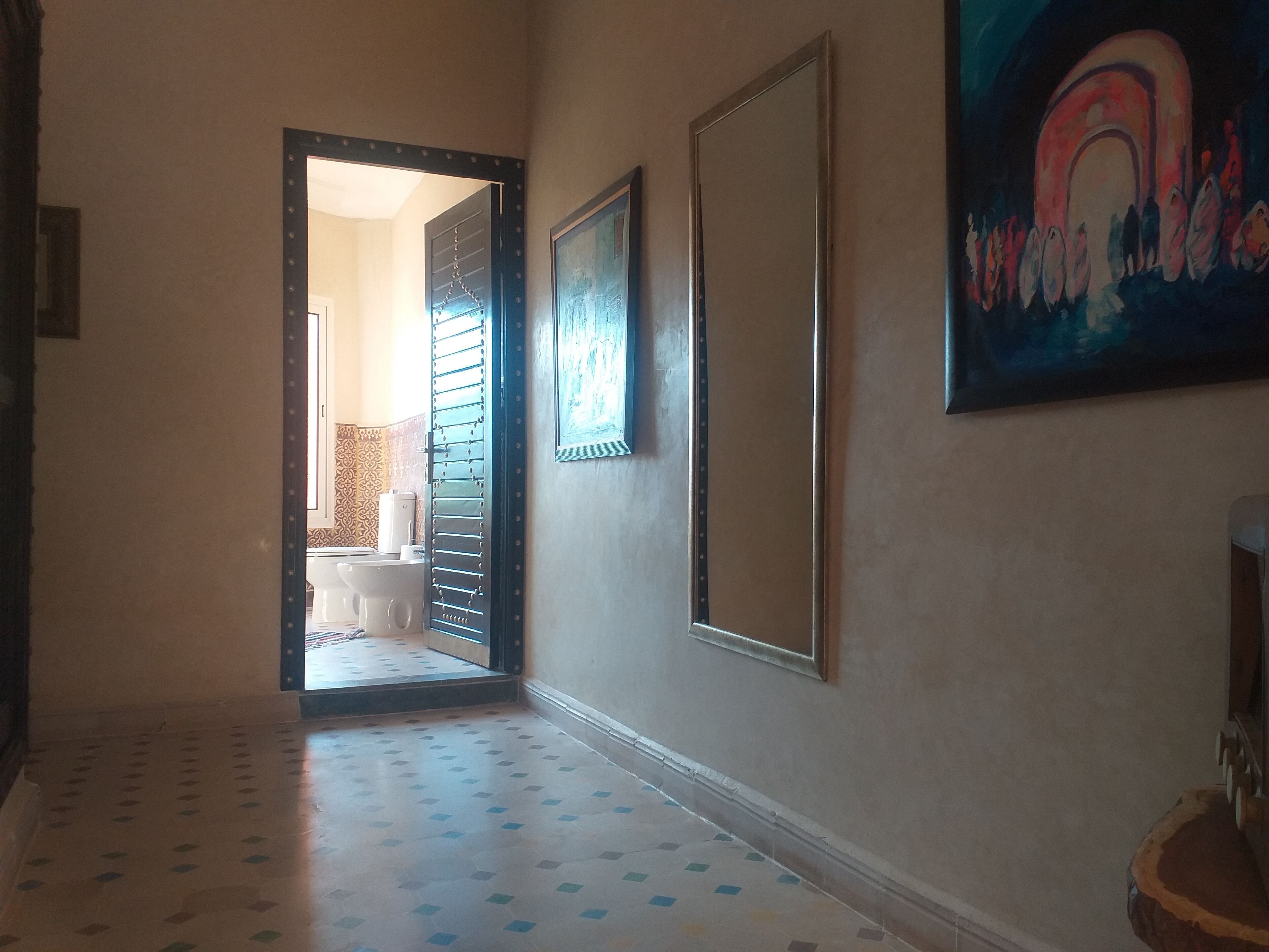 Um corredor com piso estampado, uma porta que dá para um banheiro e um quadro na parede.