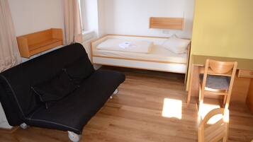 Quarto compacto com uma cama de solteiro, uma pequena escrivaninha com cadeira e um sofá.