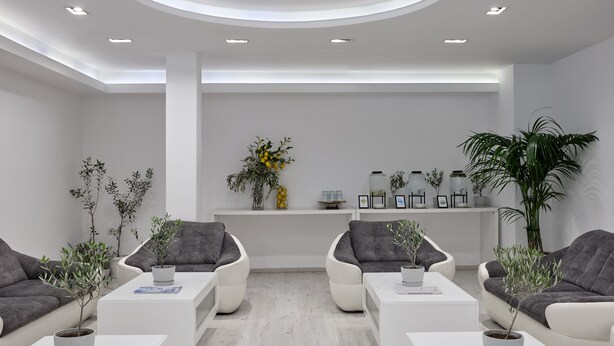 Uma área de estar moderna e minimalista, com sofás e mesas brancas, rodeada por plantas em vasos e objetos decorativos.