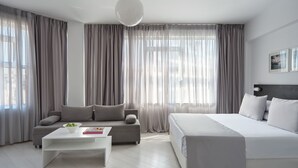 Quarto de hotel moderno com uma cama grande, um sofá, uma mesa de centro e cortinas translúcidas.