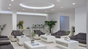 Sala de estar moderna e minimalista com sofás cinzas e mesas de centro brancas, com iluminação embutida no teto e plantas em vasos.