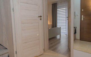 Quarto de hotel com porta de madeira, uma cama, mesa de cabeceira e janela com persianas.
