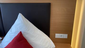 Uma cama com cabeceira preta, almofadas brancas e vermelhas, e uma tomada na parede.