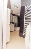 Um banheiro moderno com toucador branco, box de vidro e parede revestida de azulejos pretos.