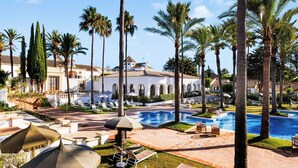 Um resort com piscina, palmeiras, espreguiçadeiras e um edifício com arcos.
