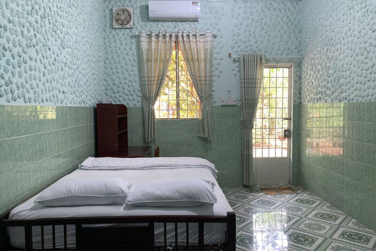 Um quarto com cama, janela com cortinas, radiador e porta.