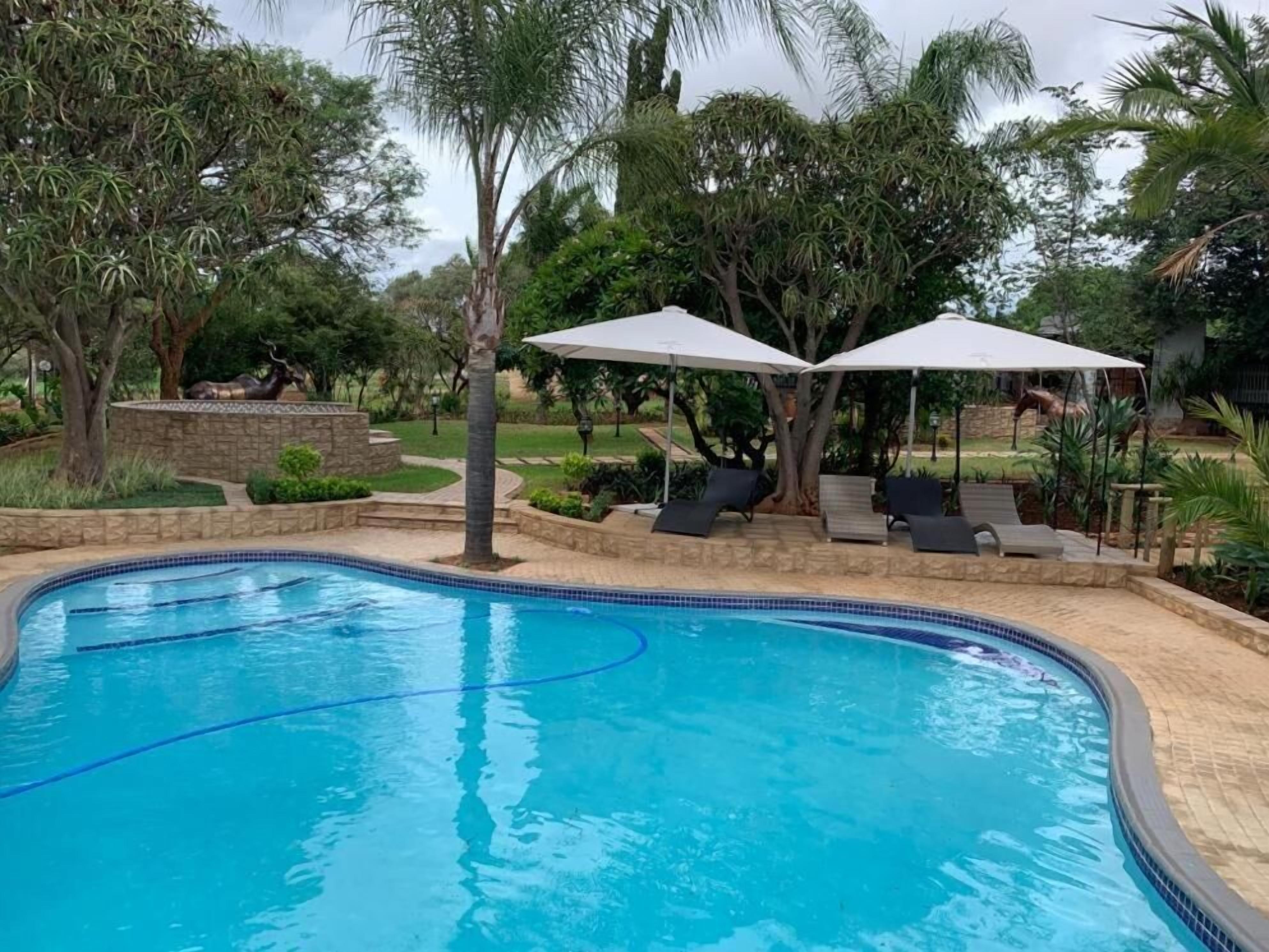 Piscina com espreguiçadeiras e guarda-sóis, cercada por vegetação e muros de pedra.