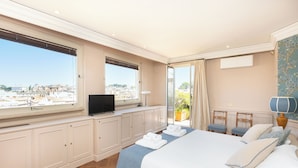 Quarto de hotel com uma cama grande, televisão numa prateleira embutida e vista para a cidade pelas janelas.