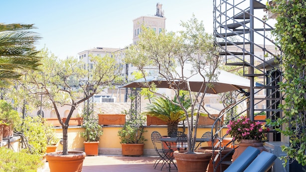 Terraço no telhado com plantas em vasos, uma mesa com cadeiras e uma área de estar com espreguiçadeiras.
