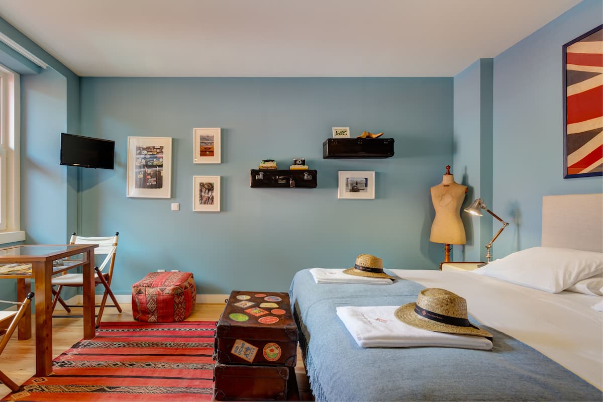 Quarto com cama, escrivaninha, cadeira, televisão e parede decorada com quadros e um manequim.