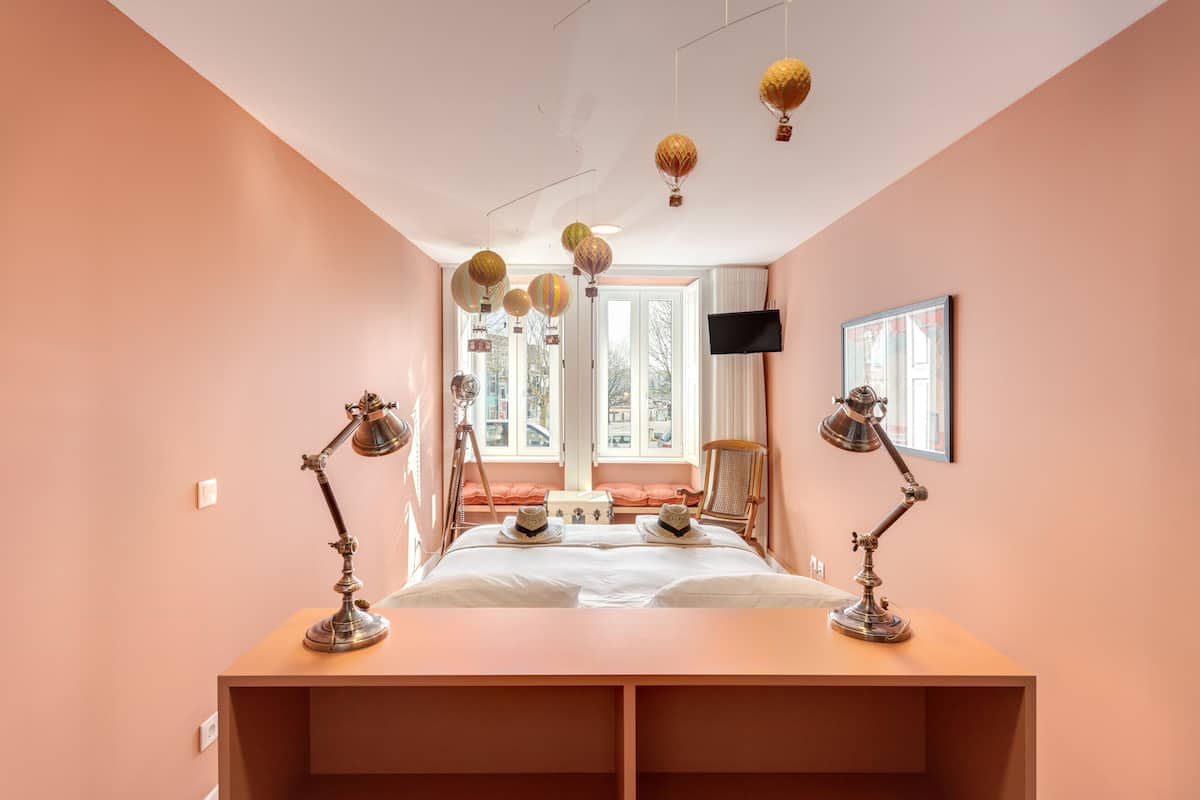 Quarto com uma cama grande, duas luminárias de cabeceira, um penteado e uma janela com vista para prédios.