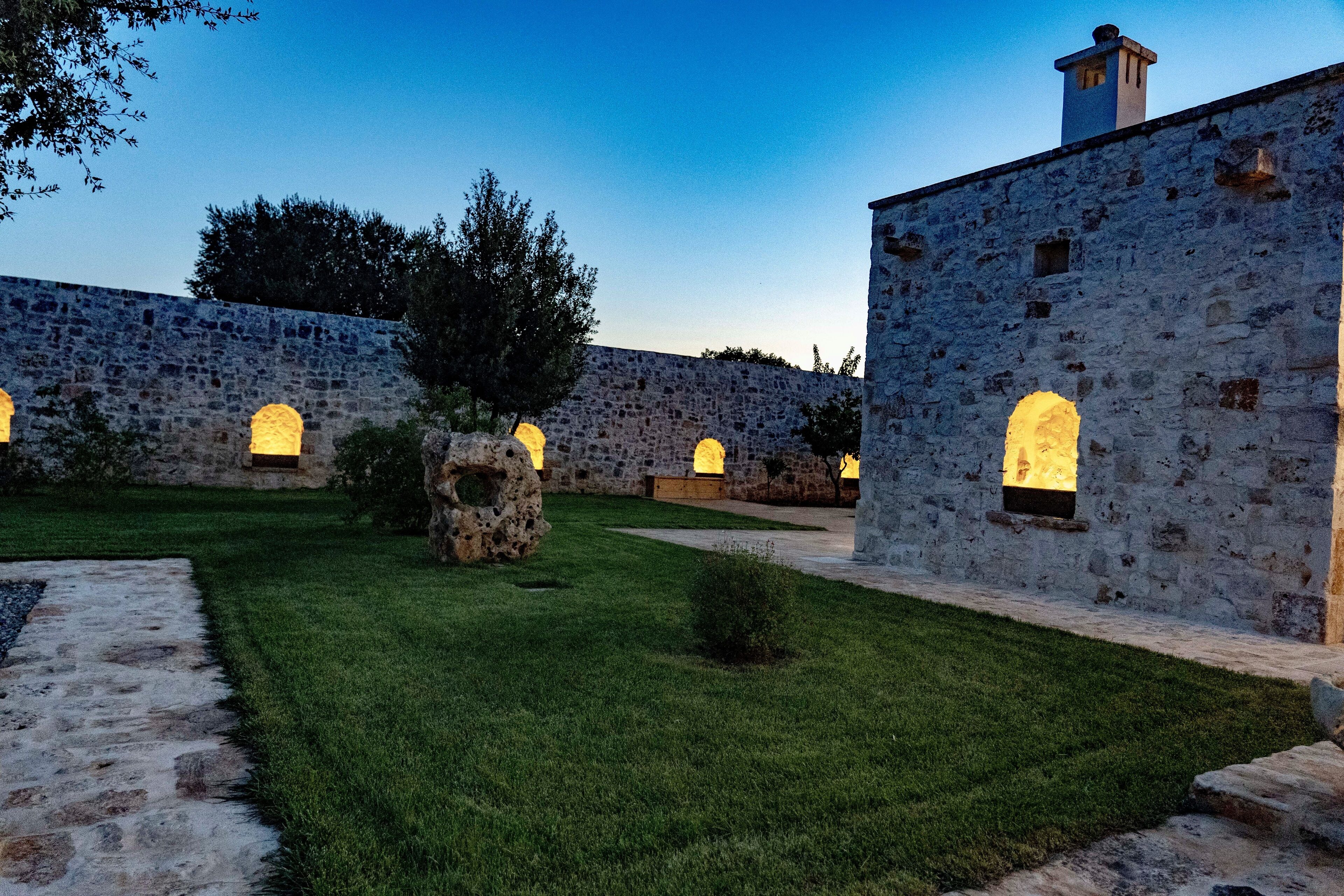 Pátio com paredes de pedra e aberturas em arco, iluminado por uma luz quente.