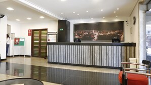Uma área de recepção moderna com um grande mural da paisagem urbana, um balcão de atendimento e uma sala de espera com cadeiras.