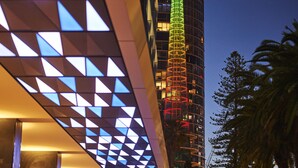 Um edifício moderno com fachada geométrica e uma torre alta com anéis iluminados.