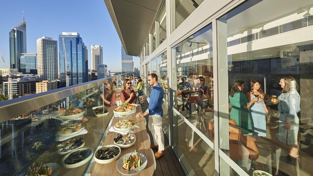 Área de refeições no terraço com vista para o horizonte da cidade, mesas ao ar livre e serviço de buffet.