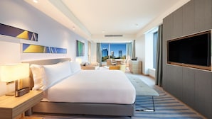 Quarto de hotel moderno com uma cama grande, televisão, escrivaninha e vista para a cidade.