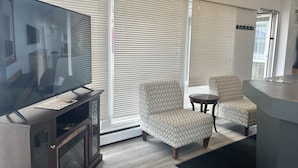 Uma sala de estar moderna com televisão de tela plana, duas poltronas estampadas, uma mesinha redonda e um rack para eletrônicos.