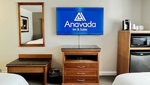 Quarto de hotel com cama, escrivaninha, cômoda, micro-ondas e televisão exibindo o logotipo do Anavada Inn & Suites.
