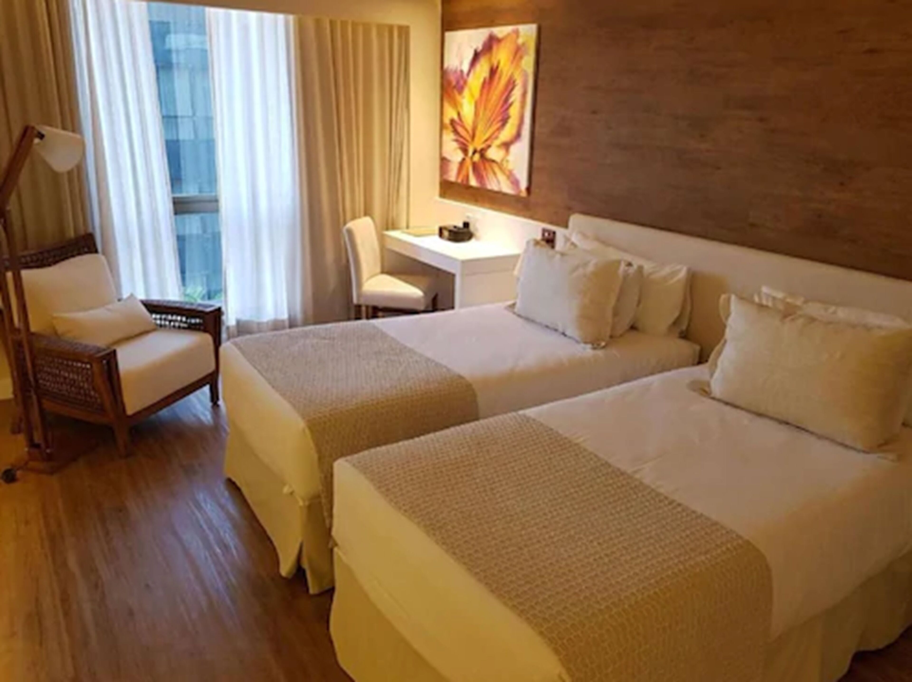 Quarto de hotel com duas camas, uma mesa, uma cadeira e uma janela com cortinas.
