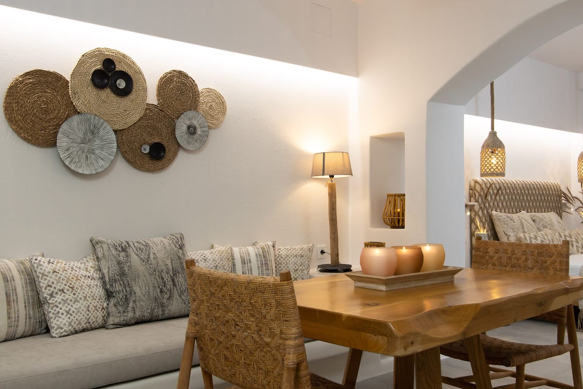 Uma sala de estar moderna com uma mesa de jantar de madeira, cadeiras de vime e um sofá com almofadas estampadas.