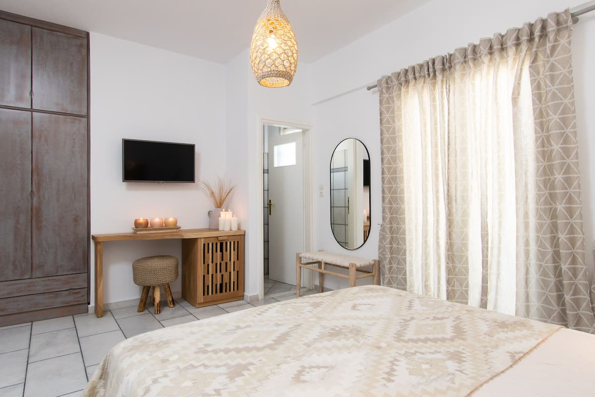 Quarto com cama, escrivaninha de madeira, televisão, espelho e guarda-roupa.
