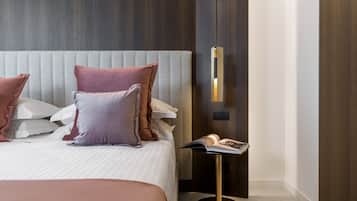 Cama bem arrumada com colcha listrada e várias almofadas, mesa de cabeceira com um livro e painel de parede moderno.