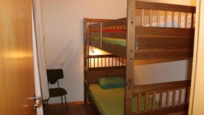 Uma cama beliche com colchão verde e travesseiro, uma cadeira de madeira e uma porta com puxador de metal.