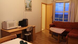Um espaço compacto com uma escrivaninha de madeira, televisão, micro-ondas, sofá e uma pequena mesa.