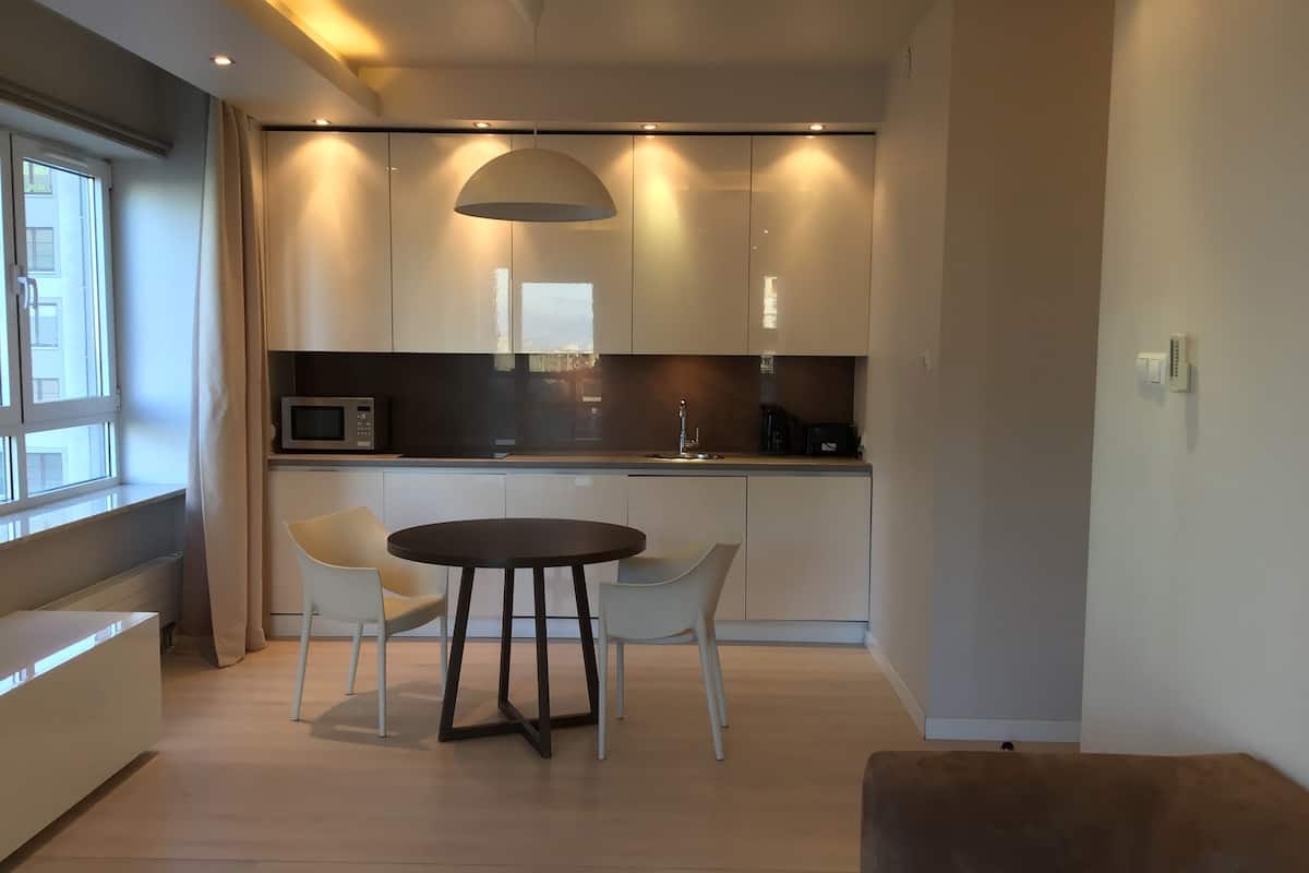Cozinha moderna com área de refeições, incluindo uma mesa redonda e cadeiras, micro-ondas e uma luminária pendente.