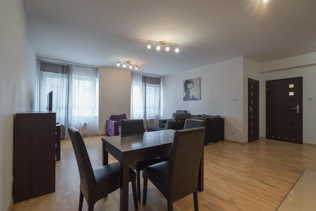 Uma sala de estar espaçosa com piso de madeira, uma mesa de jantar com cadeiras, um sofá e uma televisão.