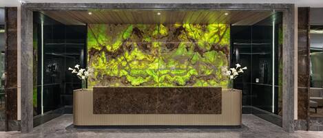 Uma área de recepção com um balcão de mármore, parede iluminada em verde e um design de teto moderno.