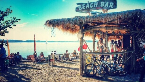 Um bar de praia com teto de palha, mesas ao ar livre e bicicletas estacionadas por perto.