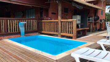 Uma piscina com deck de madeira, cerca de madeira e cadeiras de descanso brancas.