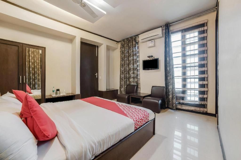 Quarto de hotel com cama, escrivaninha, cadeira, televisão e janela com persianas.