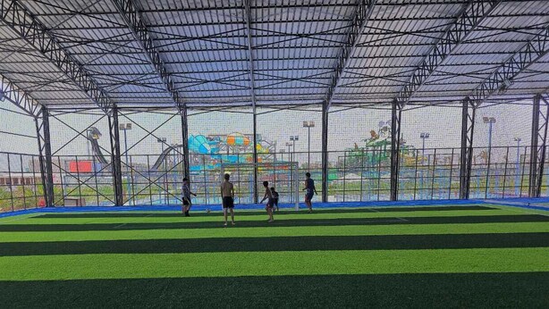 Um espaço para atividades esportivas em ambiente fechado, com área cercada por rede e grama sintética.