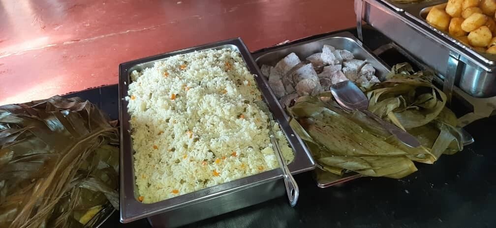 Buffet com diversos pratos, incluindo arroz, bolinhos e comida embrulhada em folhas.