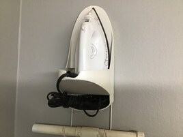 Um ferro branco numa prateleira fixada na parede, com um fio.