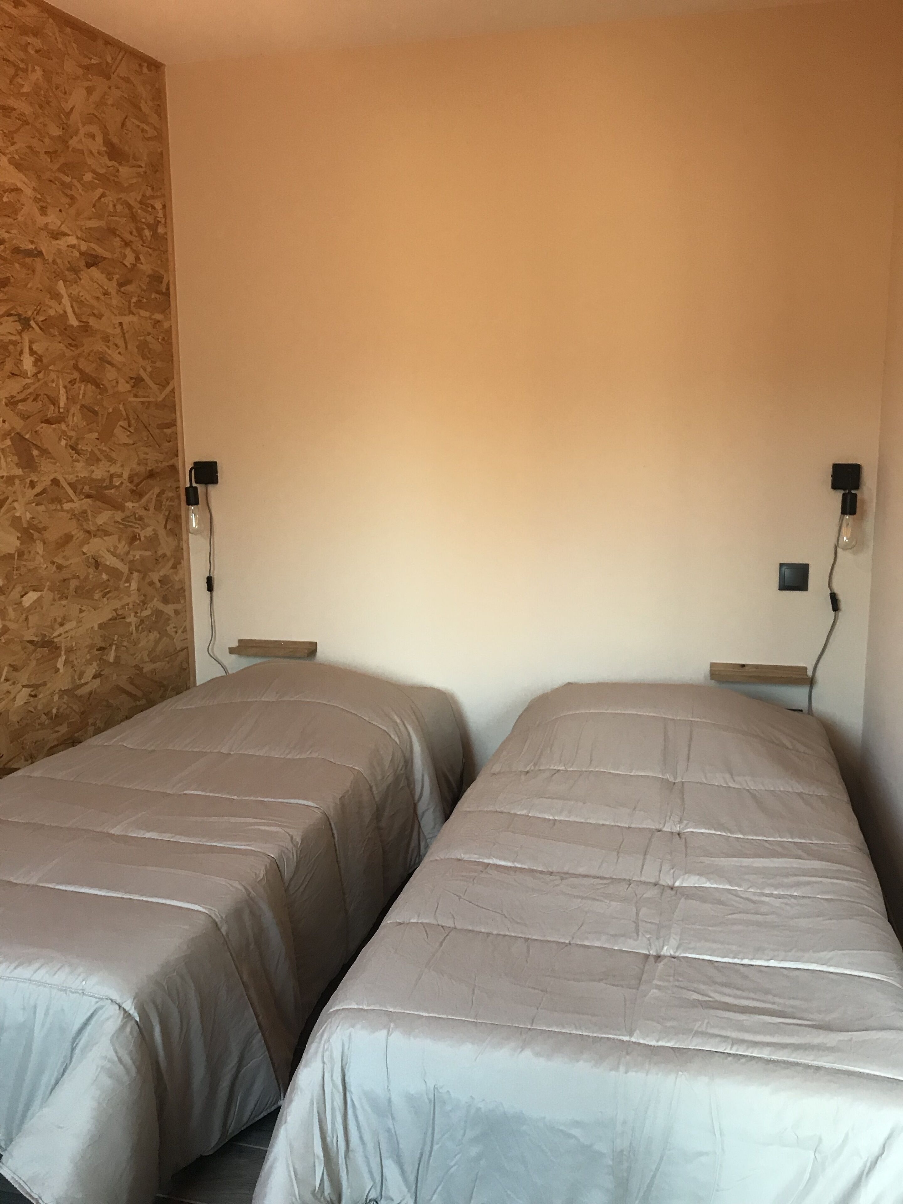 Quarto com duas camas de solteiro, painéis de parede em madeira e mesas de cabeceira com abajures.