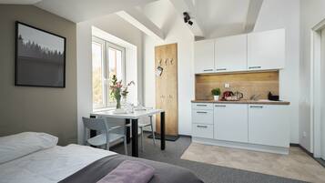 Quarto moderno com cama, escrivaninha e cozinha compacta.