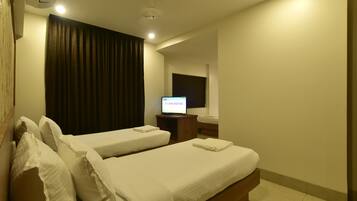 Quarto de hotel com duas camas de solteiro, televisão, escrivaninha e cortina.