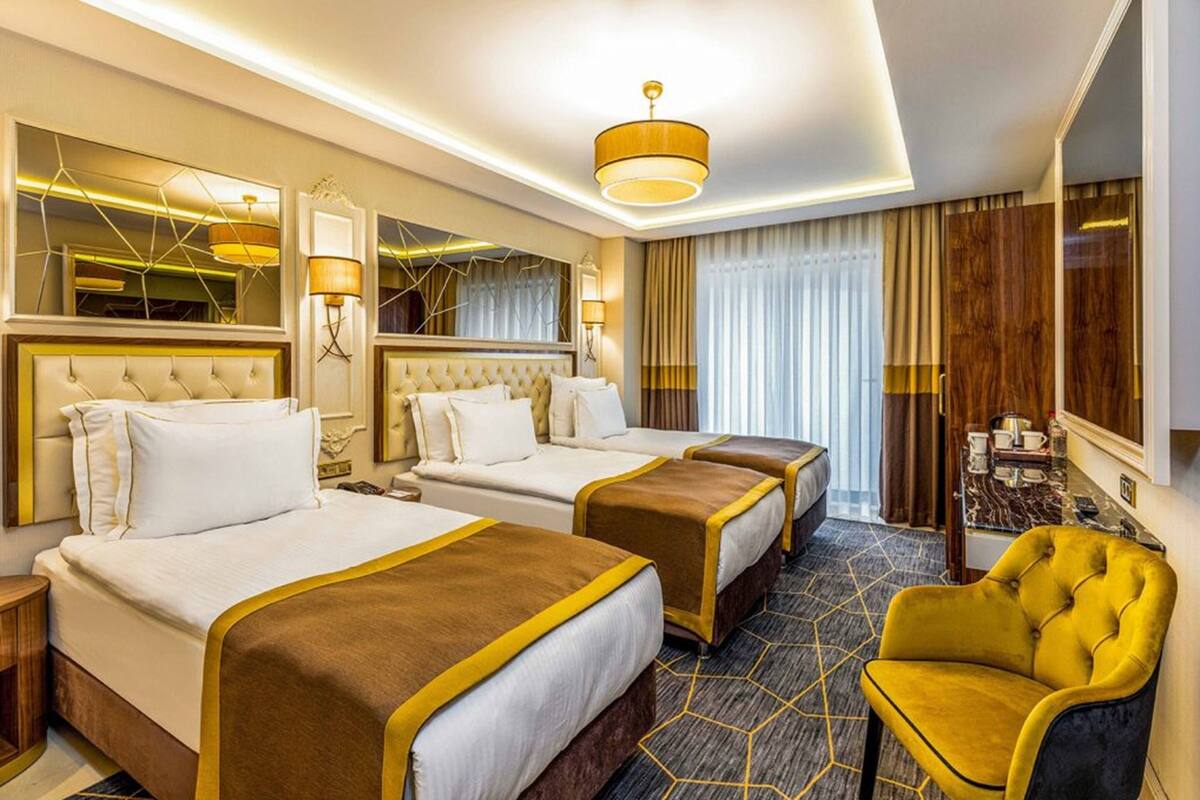 Quarto de hotel com três camas, uma poltrona amarela e um espelho grande.